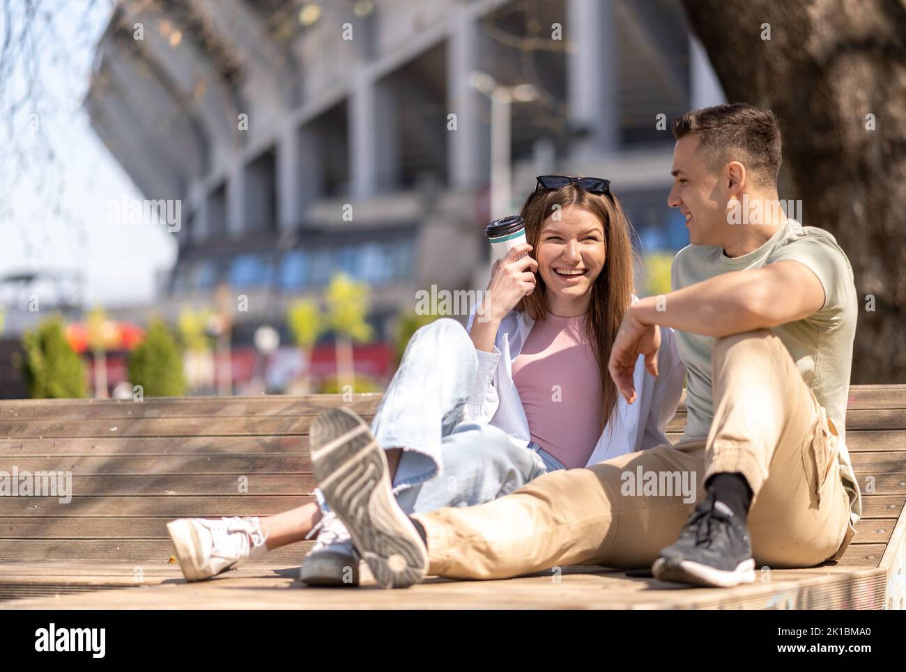 Two friends talking and laughing sitting on the bench in a park and ...