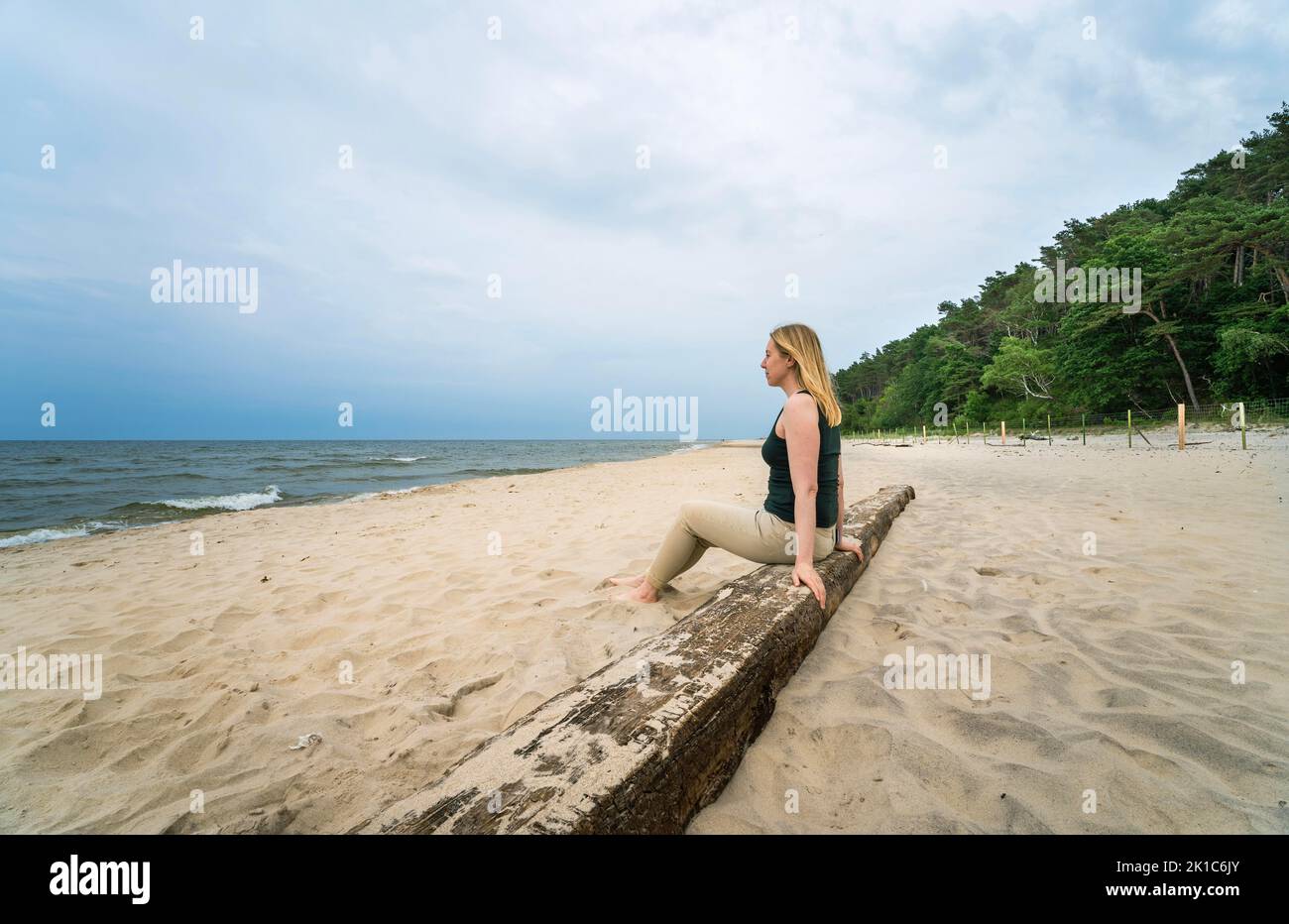 Happy woman sitting on a wooden beam at a lonely stand, Baltic Sea ...
