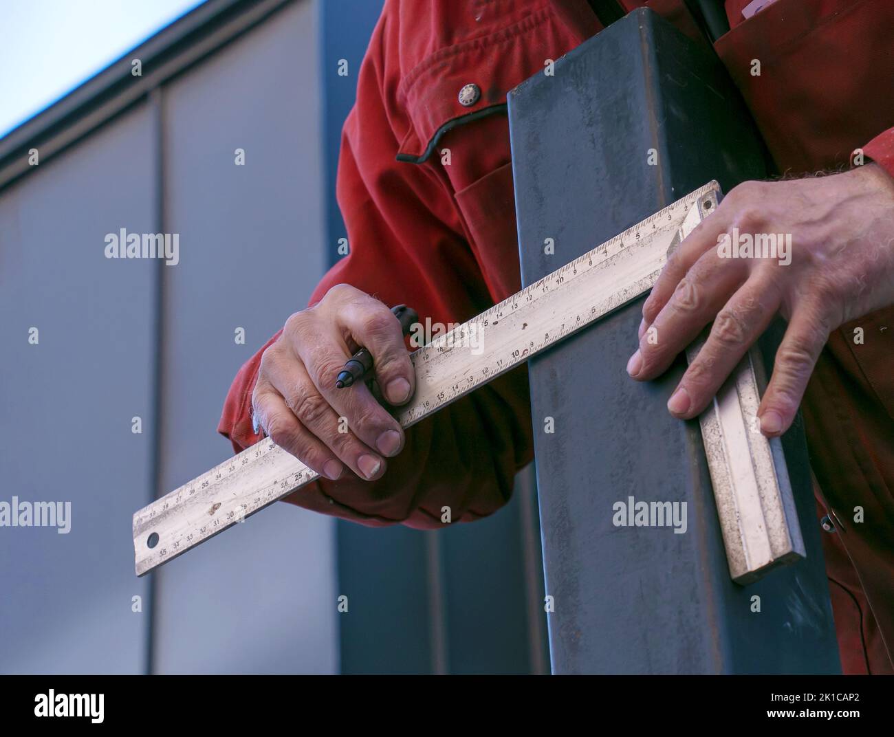 A skilled worker measures and marks a line on a square pipe with an ...