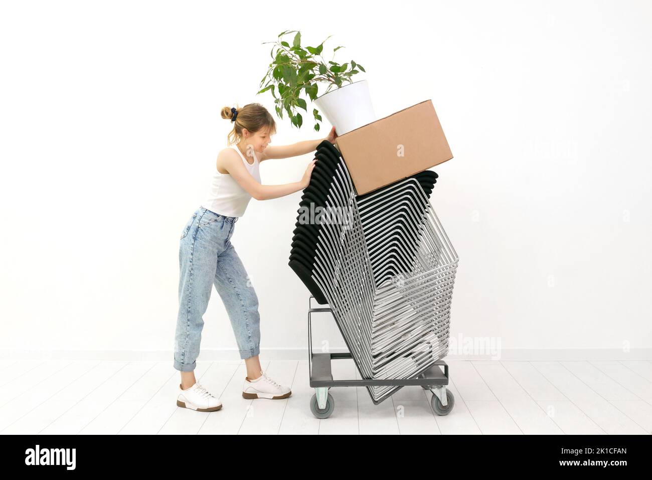 Young woman pushing a cart with chairs, a box and a flower.Moving to a ...