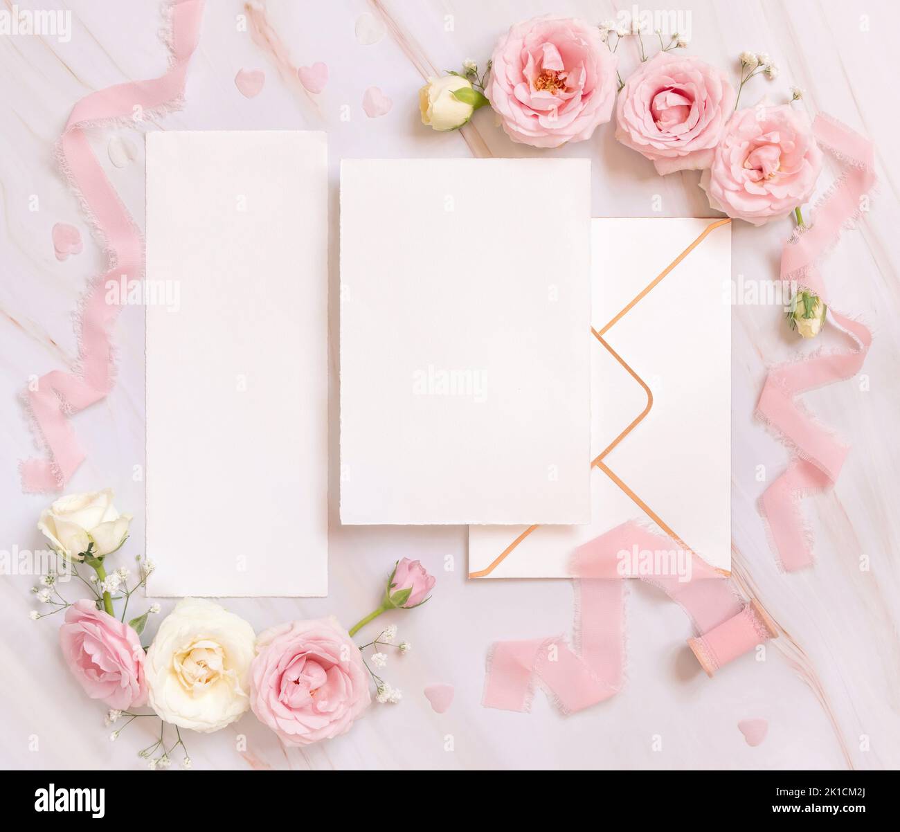 Paper cards and envelope between light pink roses and silk ribbons on ...