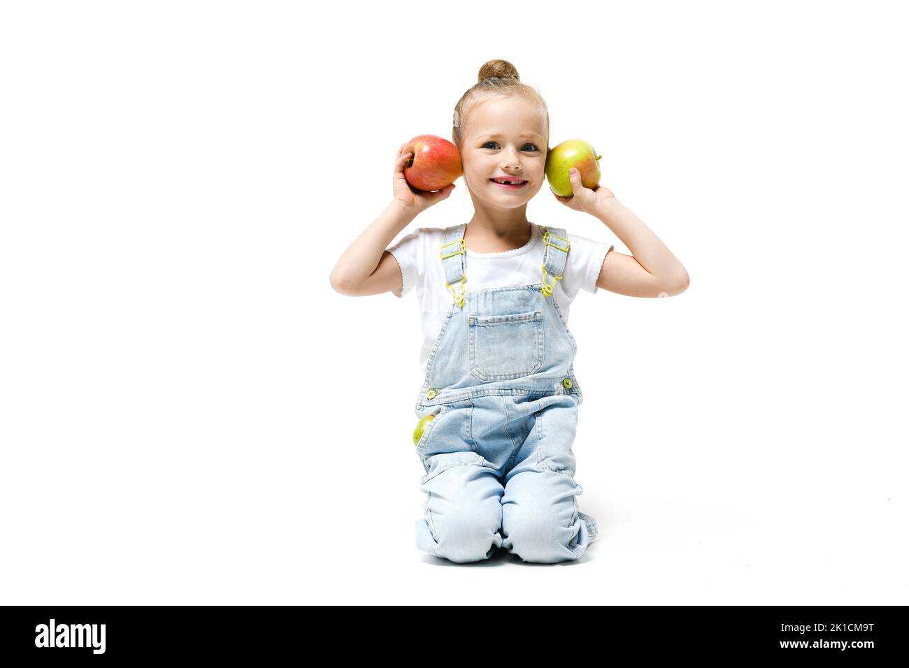 Cute girl dressed in denim overalls fooling around with apples on a ...