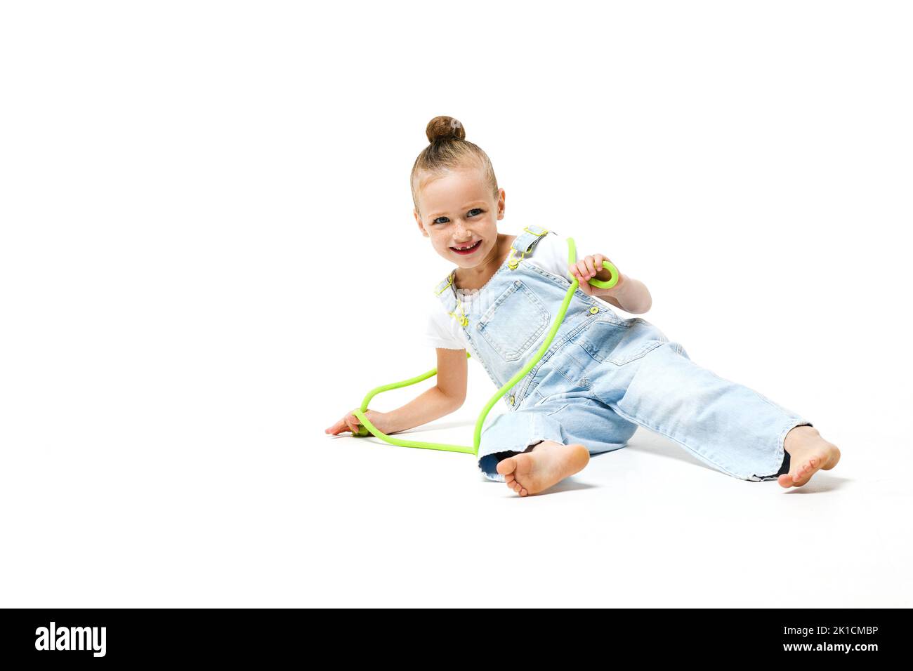 Portrait of cut little girl dressed in denim overalls with jumping rope ...