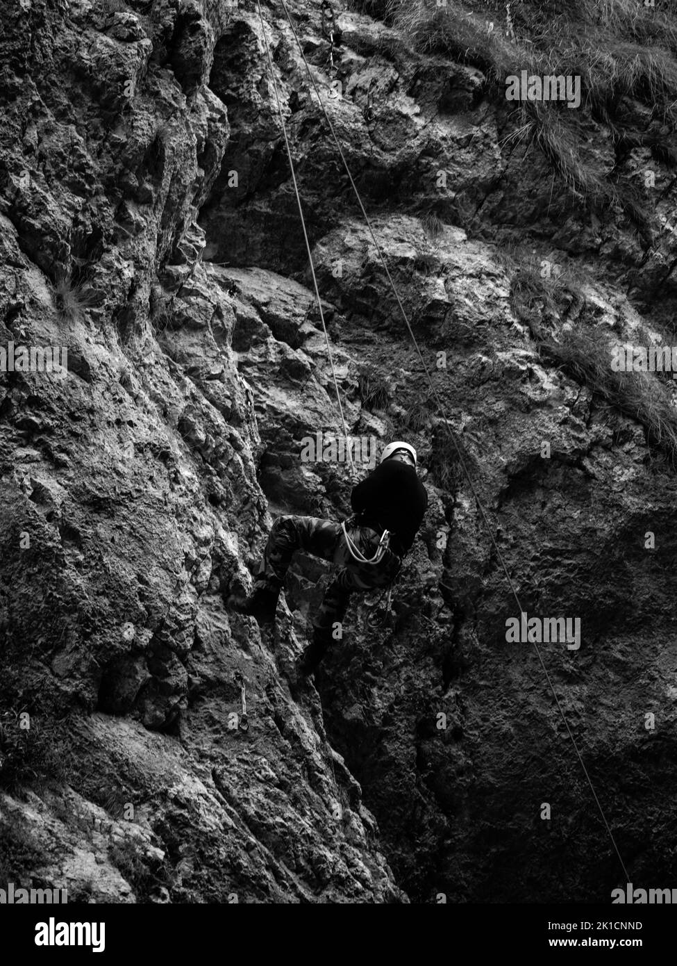 A black and white picture of a man climbing a mountain with a harness ...