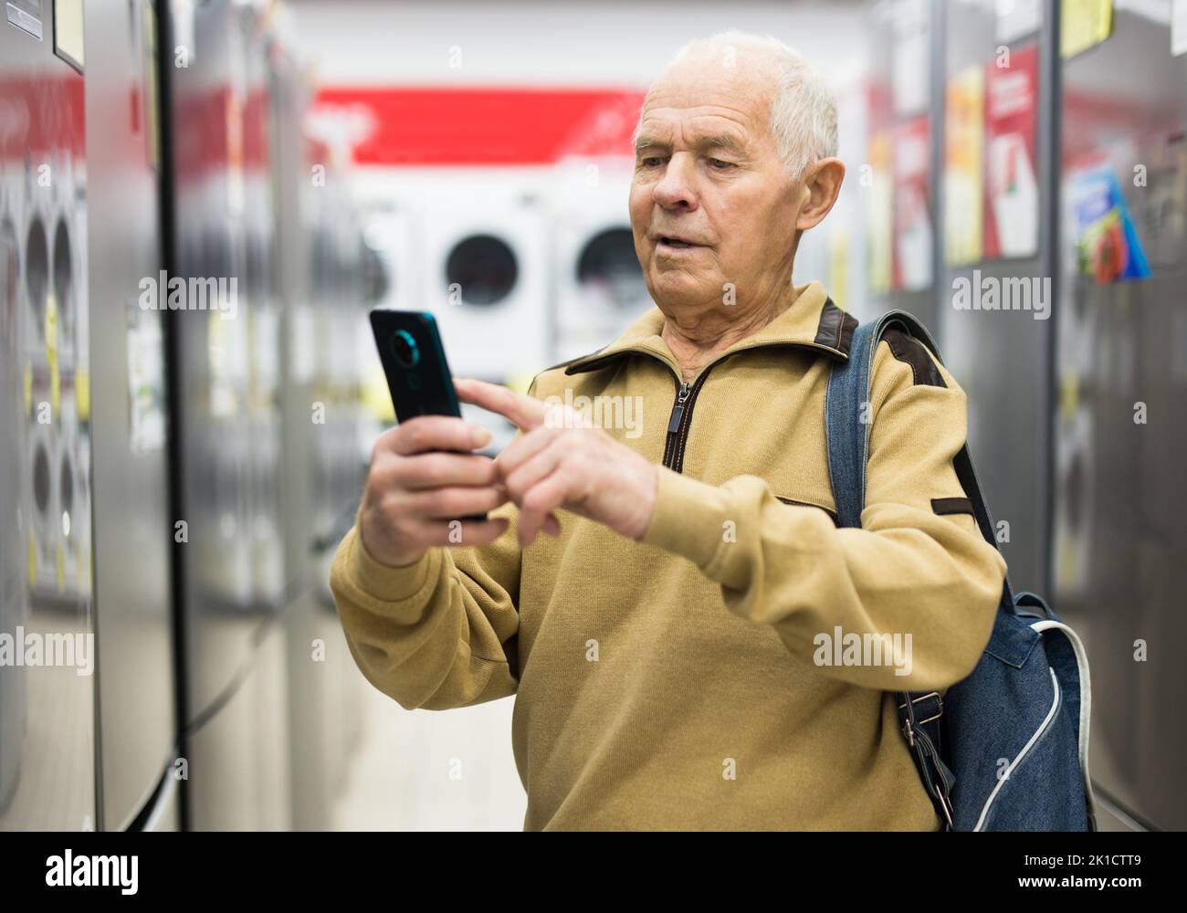elderly grayhaired man pensioner scanning QR of refrigerator at counter ...