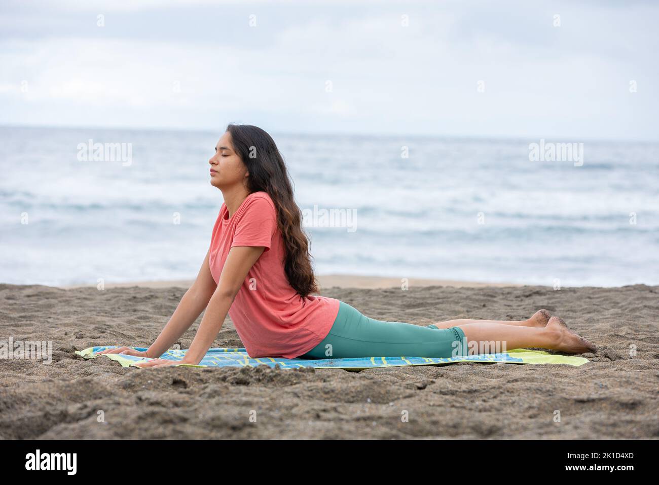 Peaceful Hispanic lady practicing Bhujangasana yoga pose on sandy ...