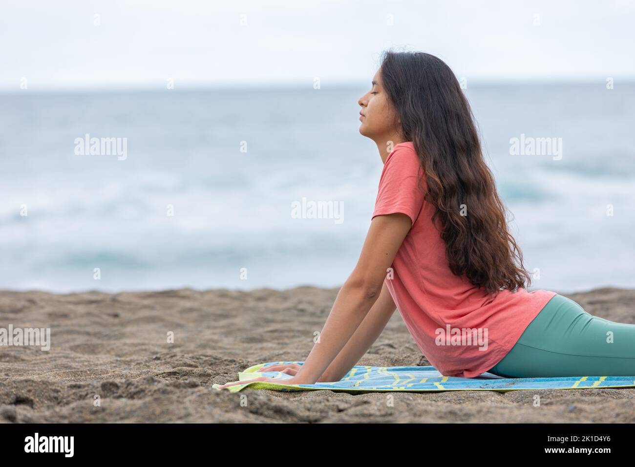 Peaceful Hispanic lady practicing Bhujangasana yoga pose on sandy ...