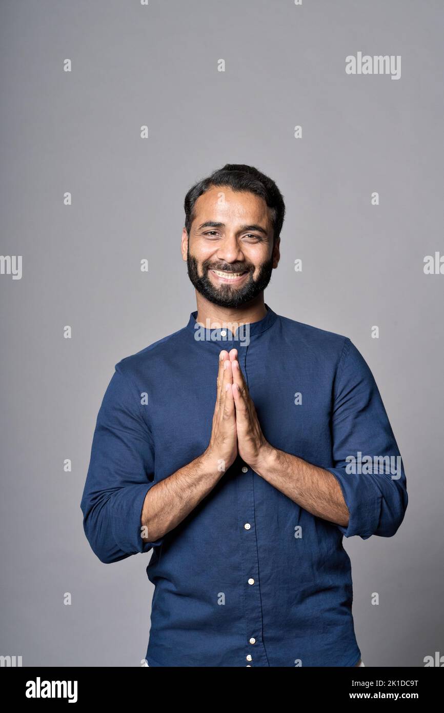 Happy indian man meditating holding hands in namaste isolated on gray ...
