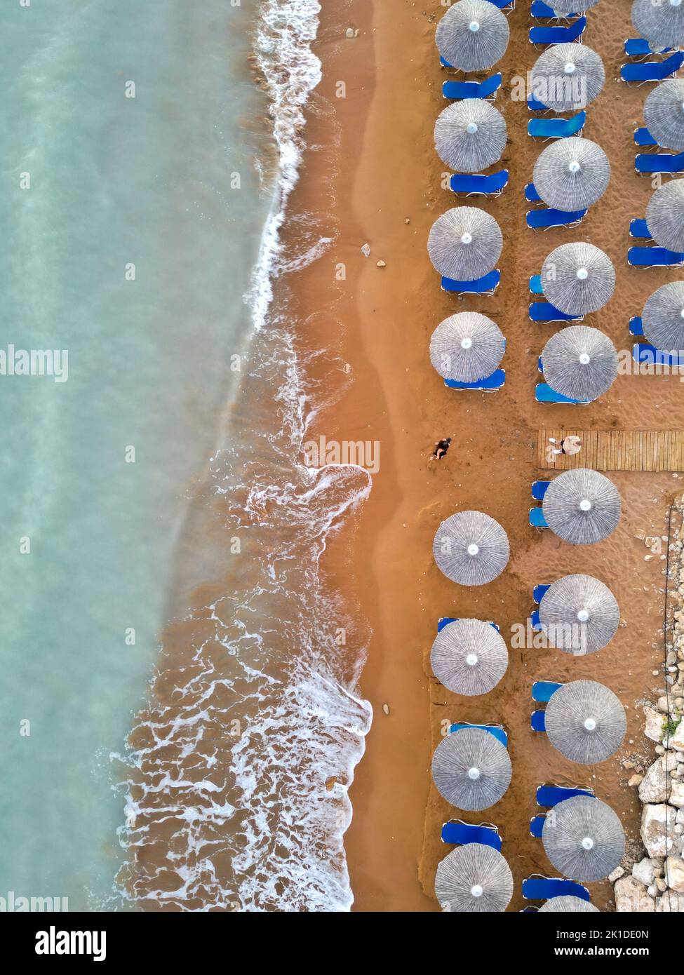 A scenic top view of a sand beach with umbrellas and the waves hitting ...