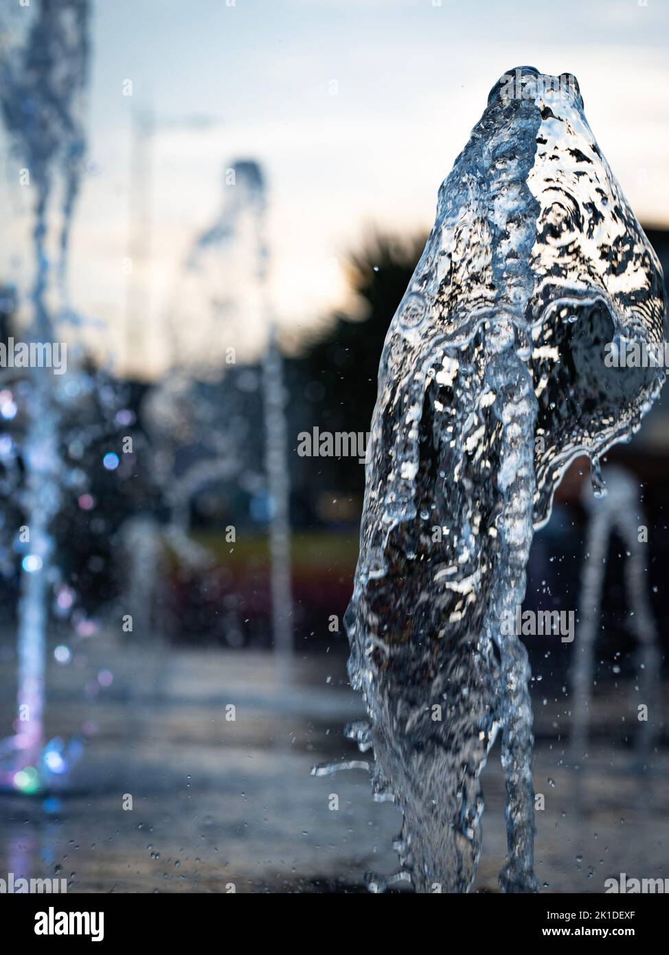 A vertical shot of fountain water splashing on a blurry background ...
