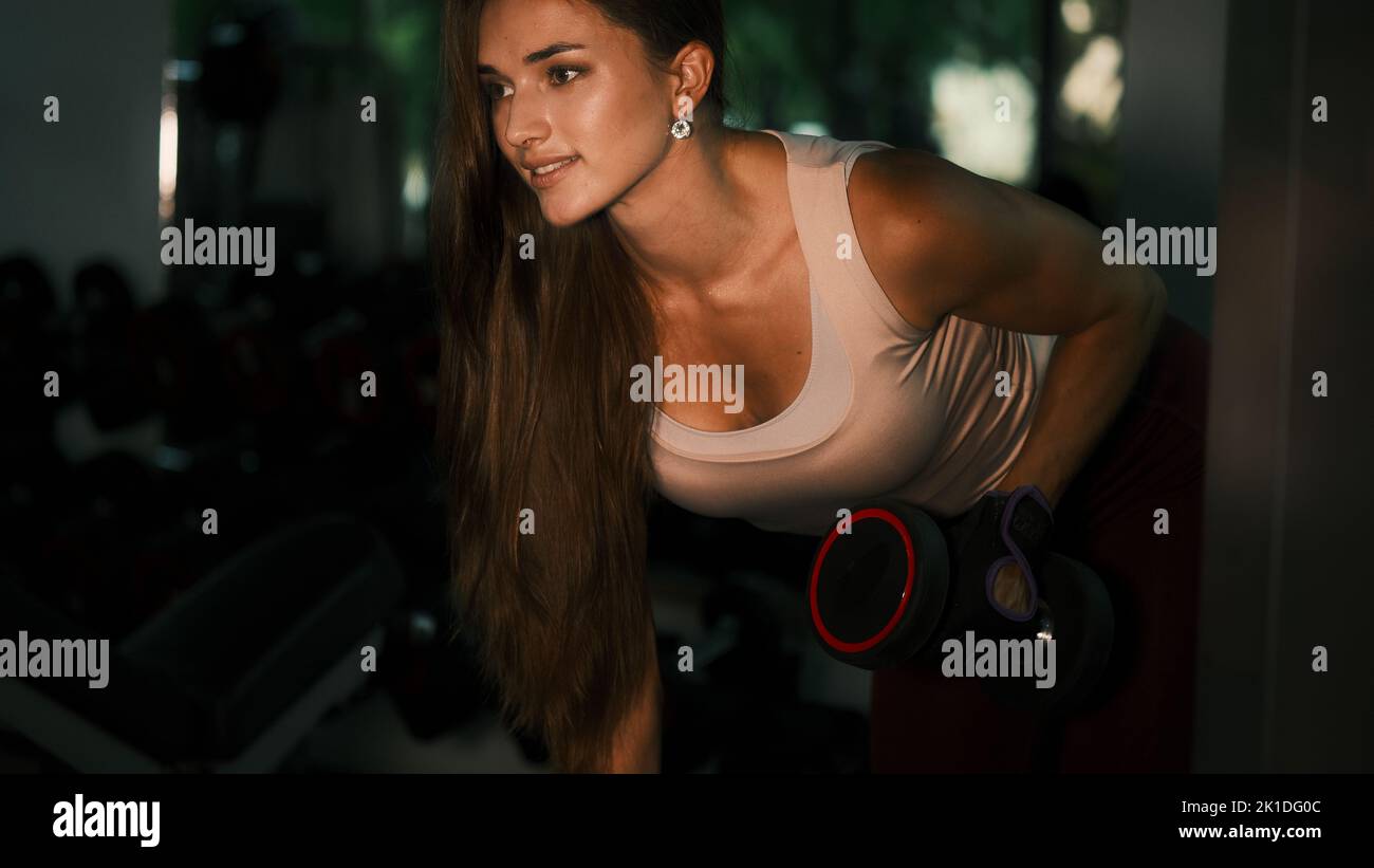 The girl lifts a dumbbell with her left hand in an inclination Stock ...