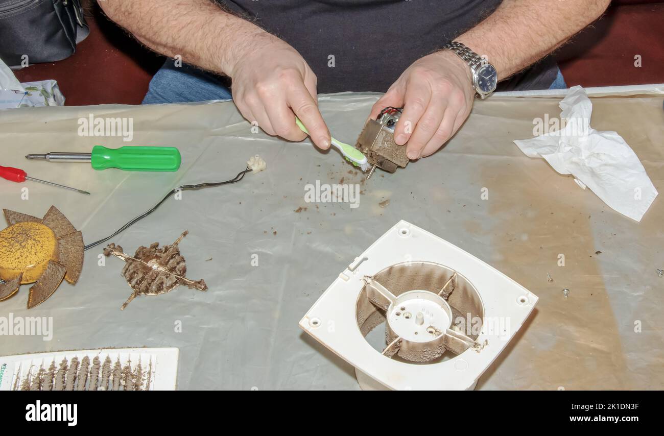 Cleaning a very dirty kitchen exhaust fan from dirt with a brush. A man ...