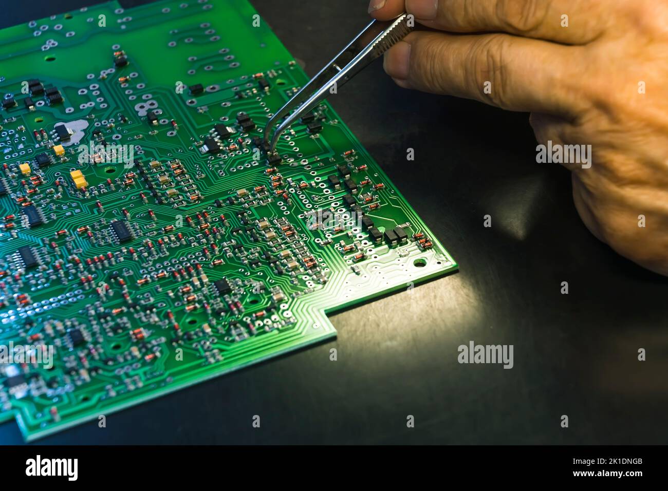 Hand gripping tweezers assembling electrical parts on detailed surface ...