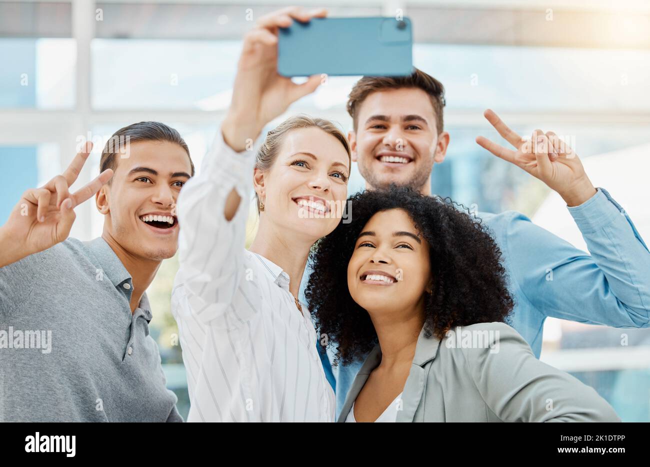 Business people talking selfie on mobile phone at work, peace hand sign and happiness during ...