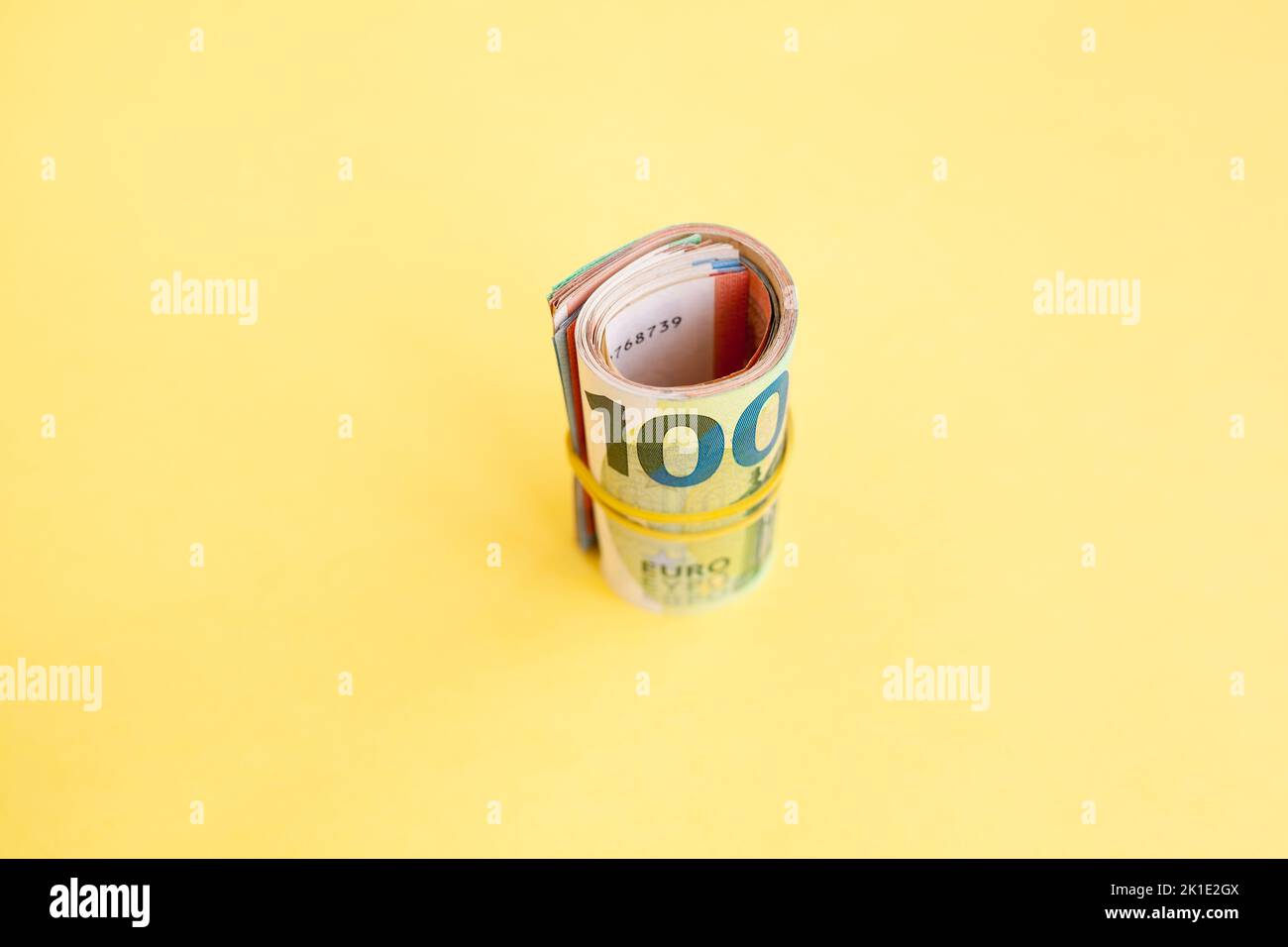 Money roll of euro banknotes with yellow rubber band on yellow ...