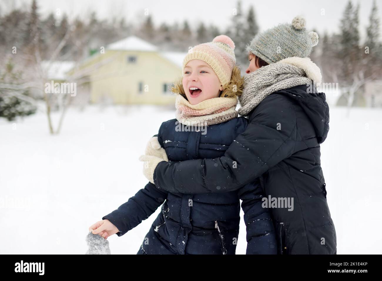 Two young sisters having fun on a walk in snow covered park on chilly ...