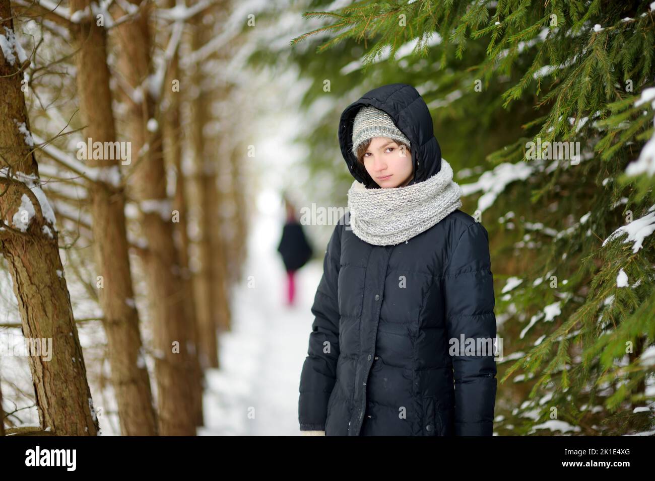 Cute young girl having fun on a walk in snow covered pine forest on ...