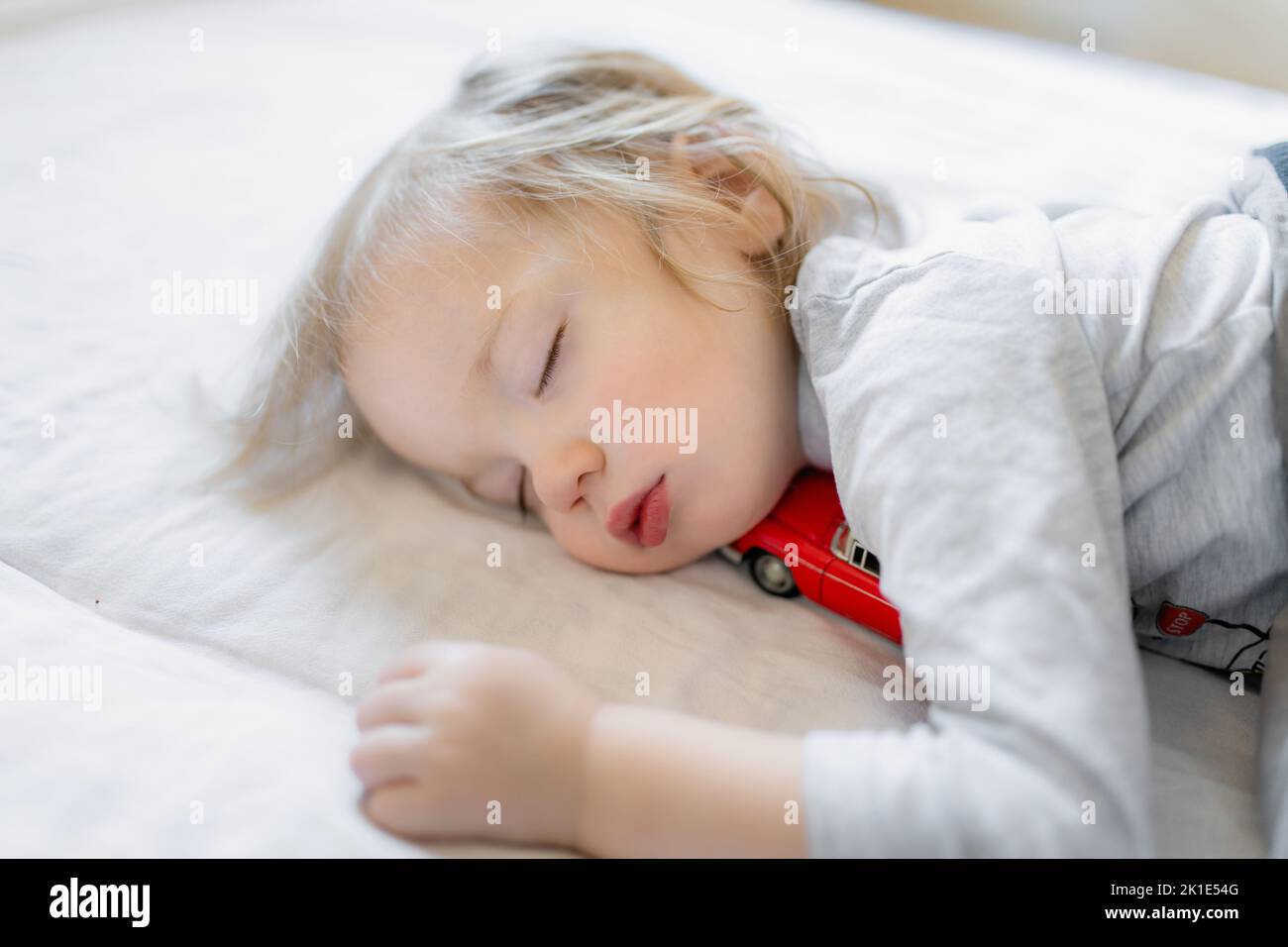 Adorable toddler boy sleeping in bed with his toy car. Tired child ...