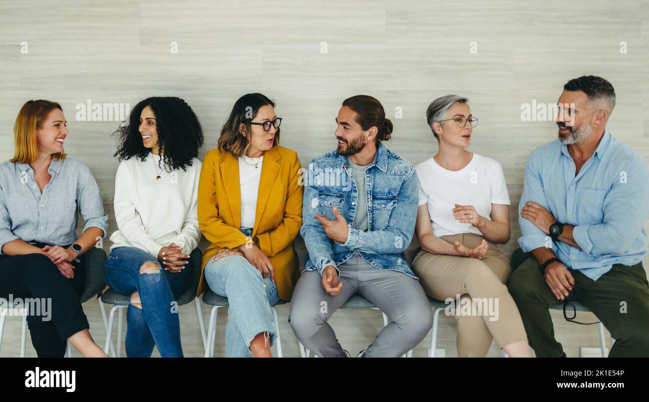 Cheerful businesspeople talking to each other while sitting in line for ...