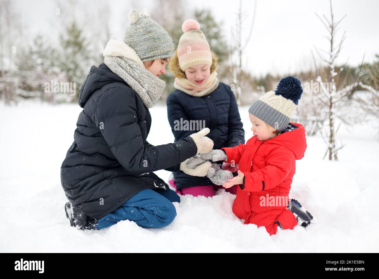 Two cute young sisters and their toddler brother having fun in snow ...