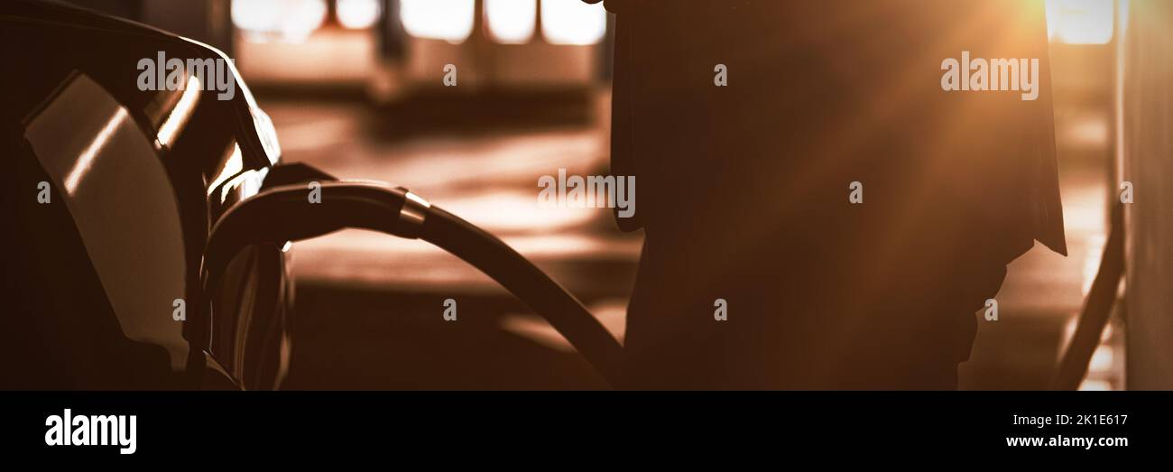 Businessman using mobile phone while charging electric car at charging ...