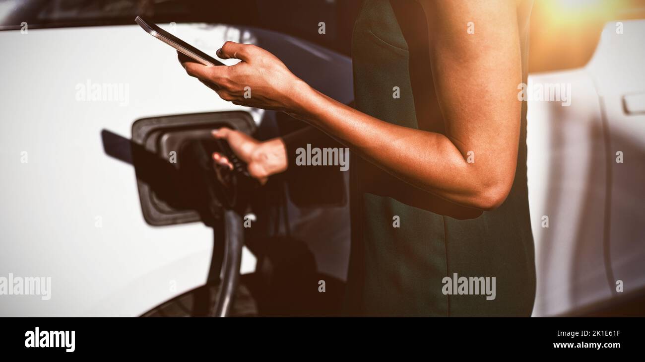 Mid section of woman using mobile phone while charging electric car at ...