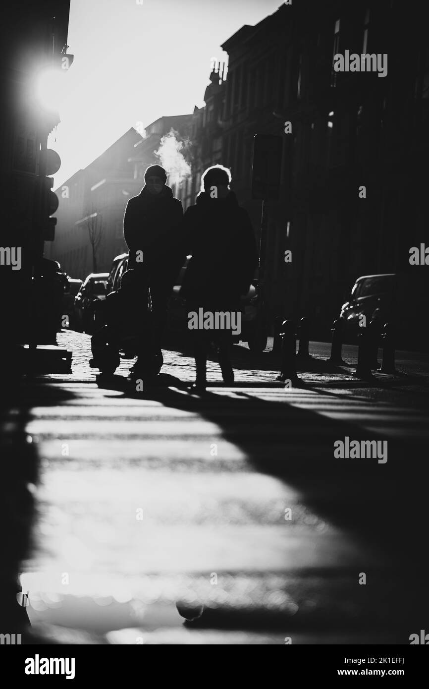 Two people walking on a street with shadow on the surface, grayscale ...