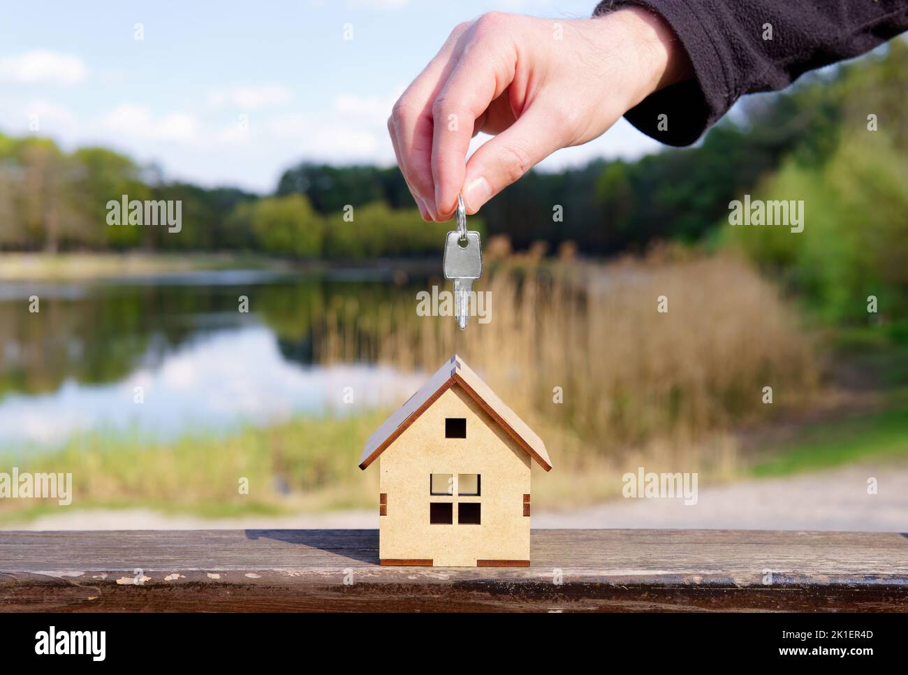 Male hand holding a house key above a toy wooden home model placed ...