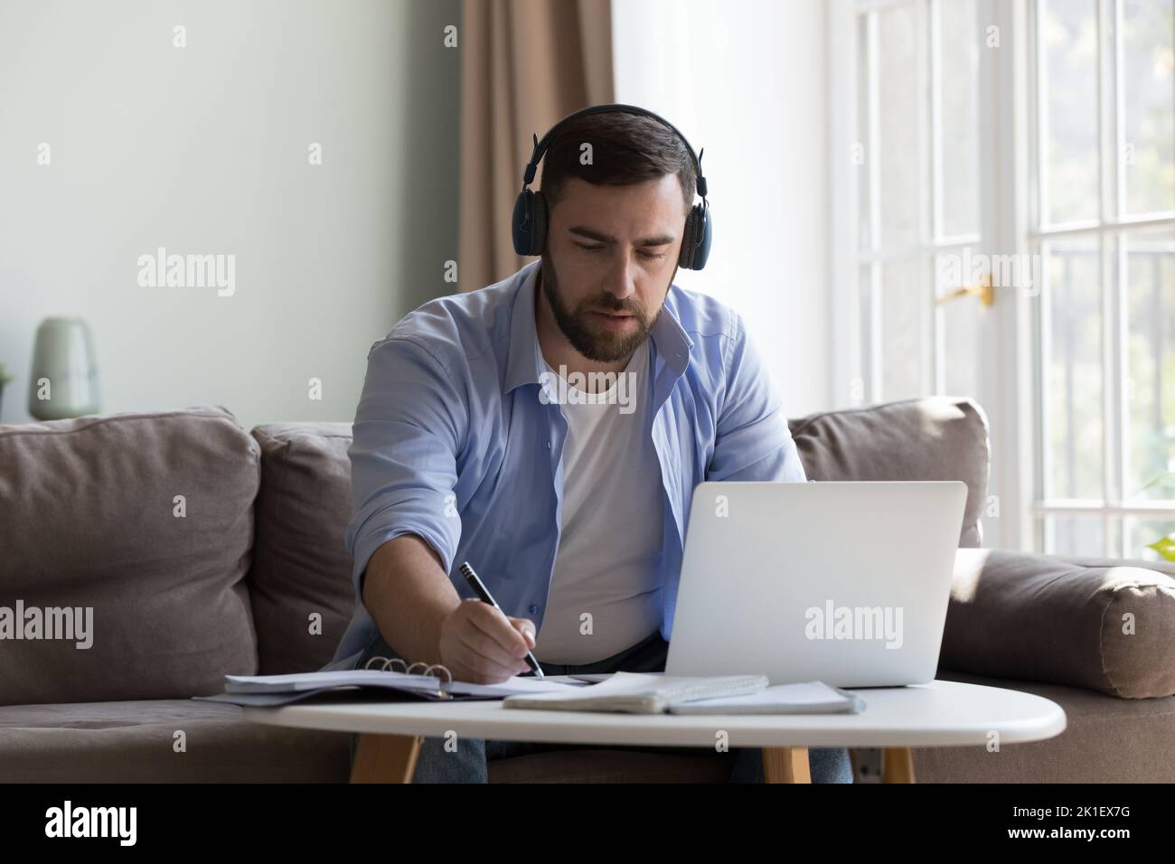 Focused serious millennial man in wireless headphones talking video ...