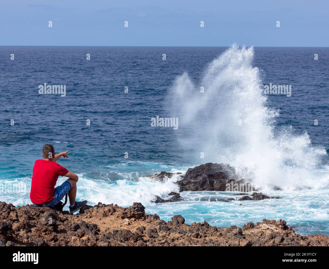 A beautiful shot of an ocean wave hitting the rock viewed by a man ...