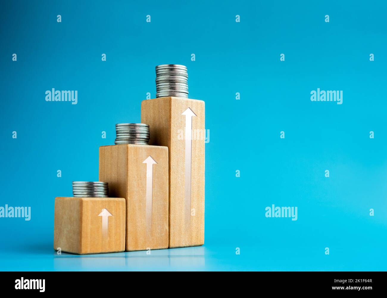 Shining rise up arrow on wooden cube blocks top with coins stacked, bar graph chart steps on ...
