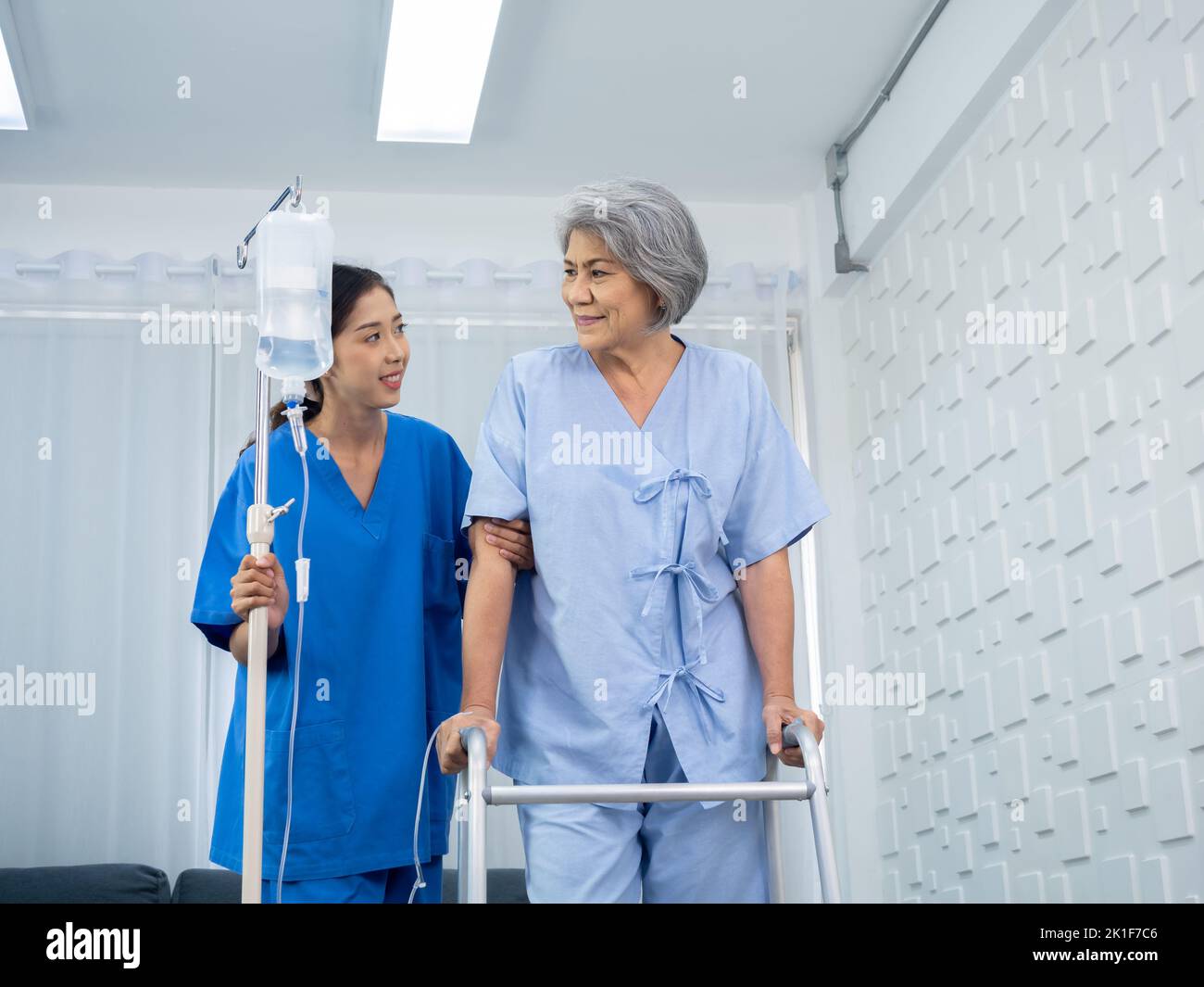 Elderly Asian woman patient trying to walk on walking frame held and ...