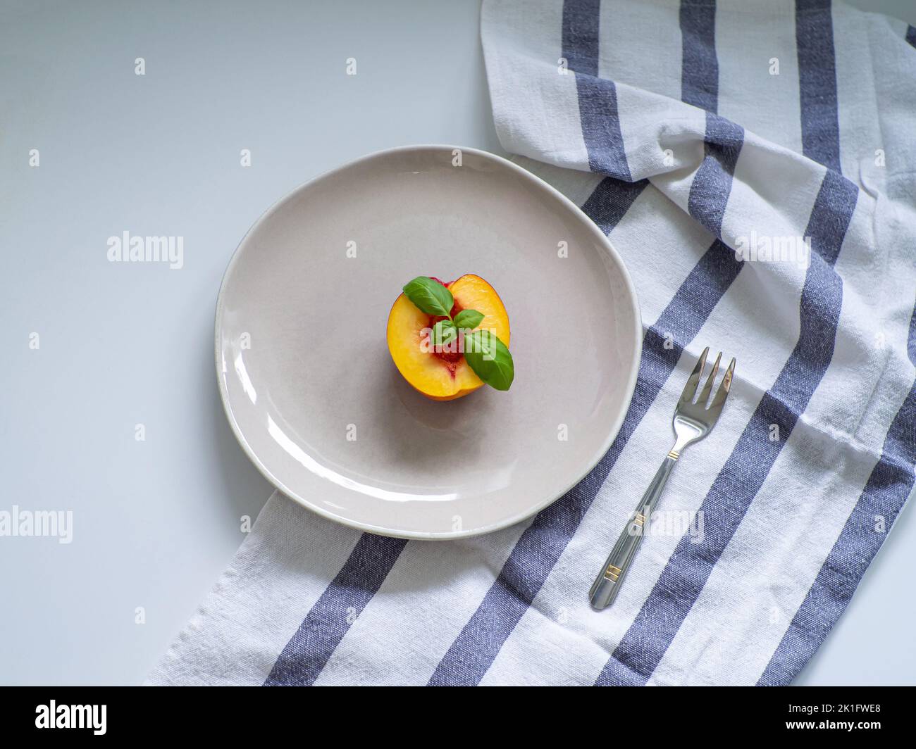 nectarine and green basil on the beige plate with fork on white table ...