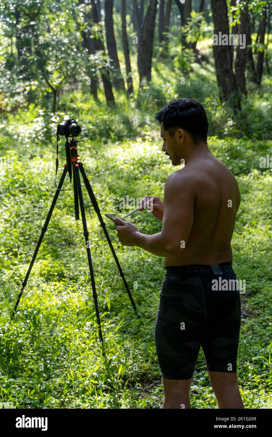 A young Hispanic athletic man video blogging in a forest before or ...