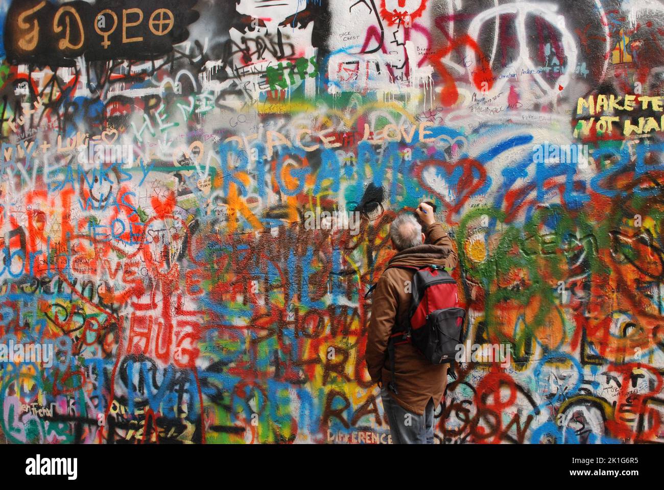 A man with a backpack spray painting graffiti on the John Lennon Wall ...