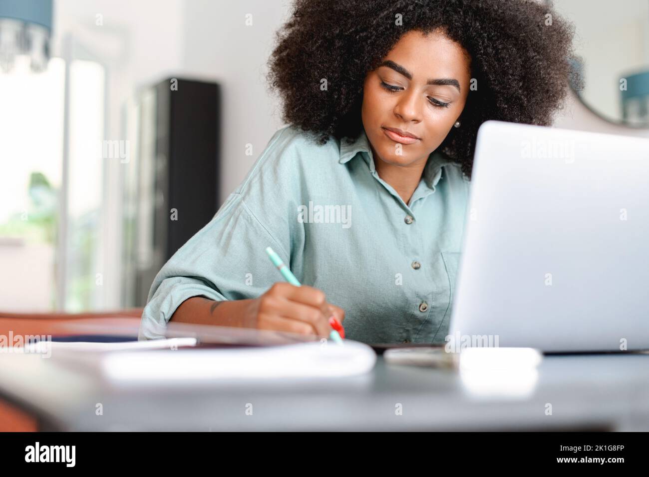 Female student watching lecture, webinar using laptop, sits at table ...