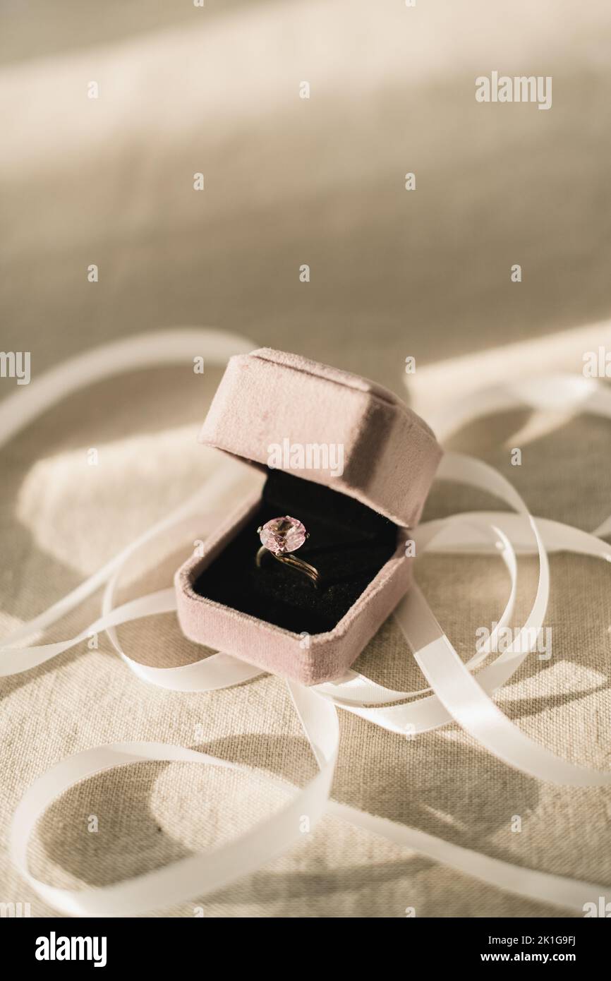 A vertical shot of a pink diamond ring in a velvet box and ribbon on a ...
