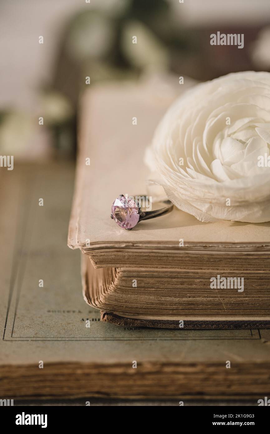 A vertical shot of a pink diamond ring underneath a white rose flower ...