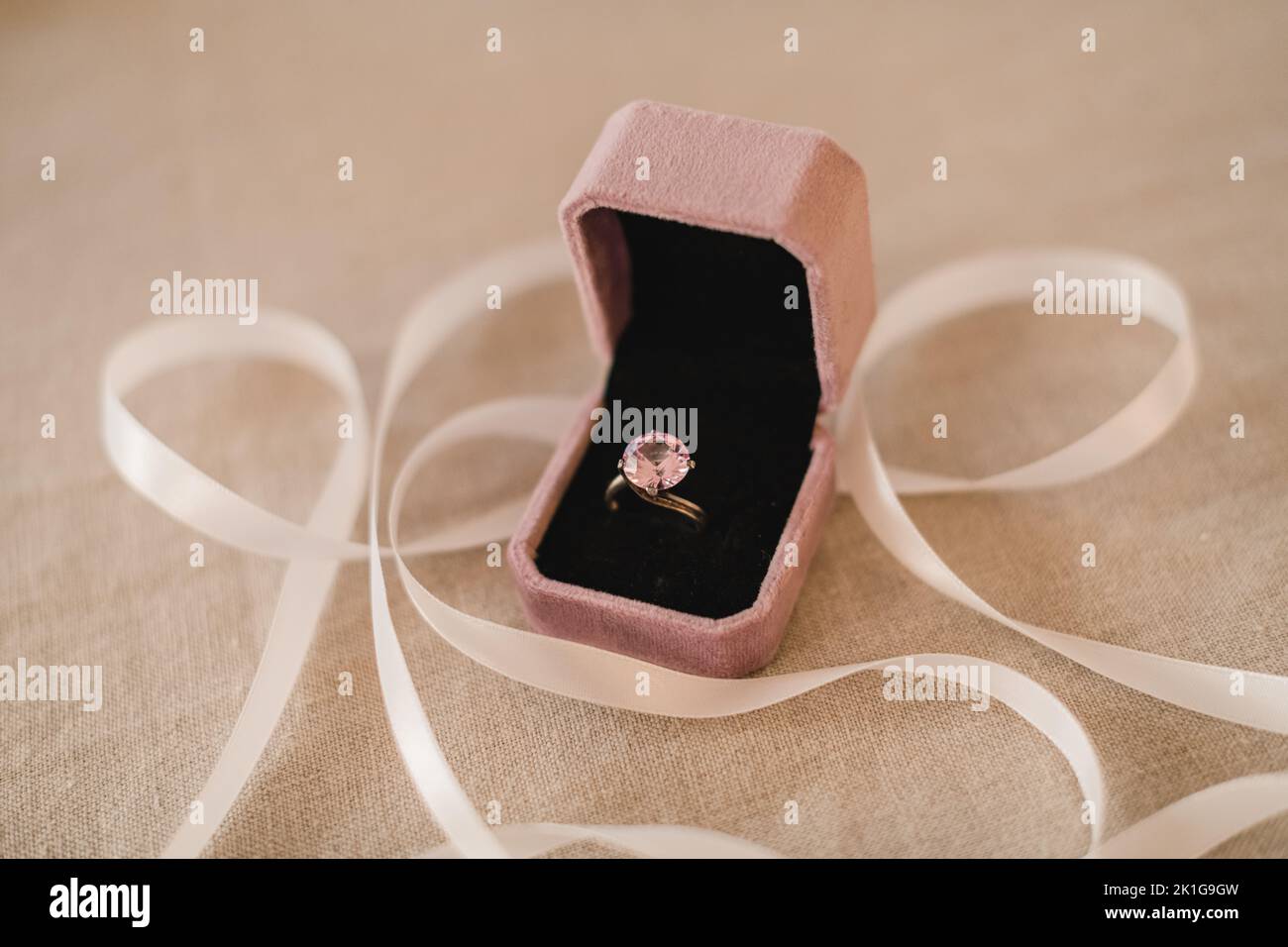 A closeup of a pink diamond ring in a velvet box and ribbon on a burlap ...