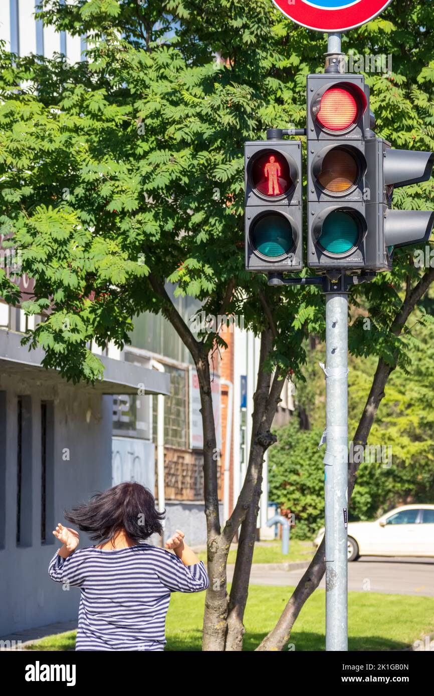 A black traffic light with a person and green trees around next to ...