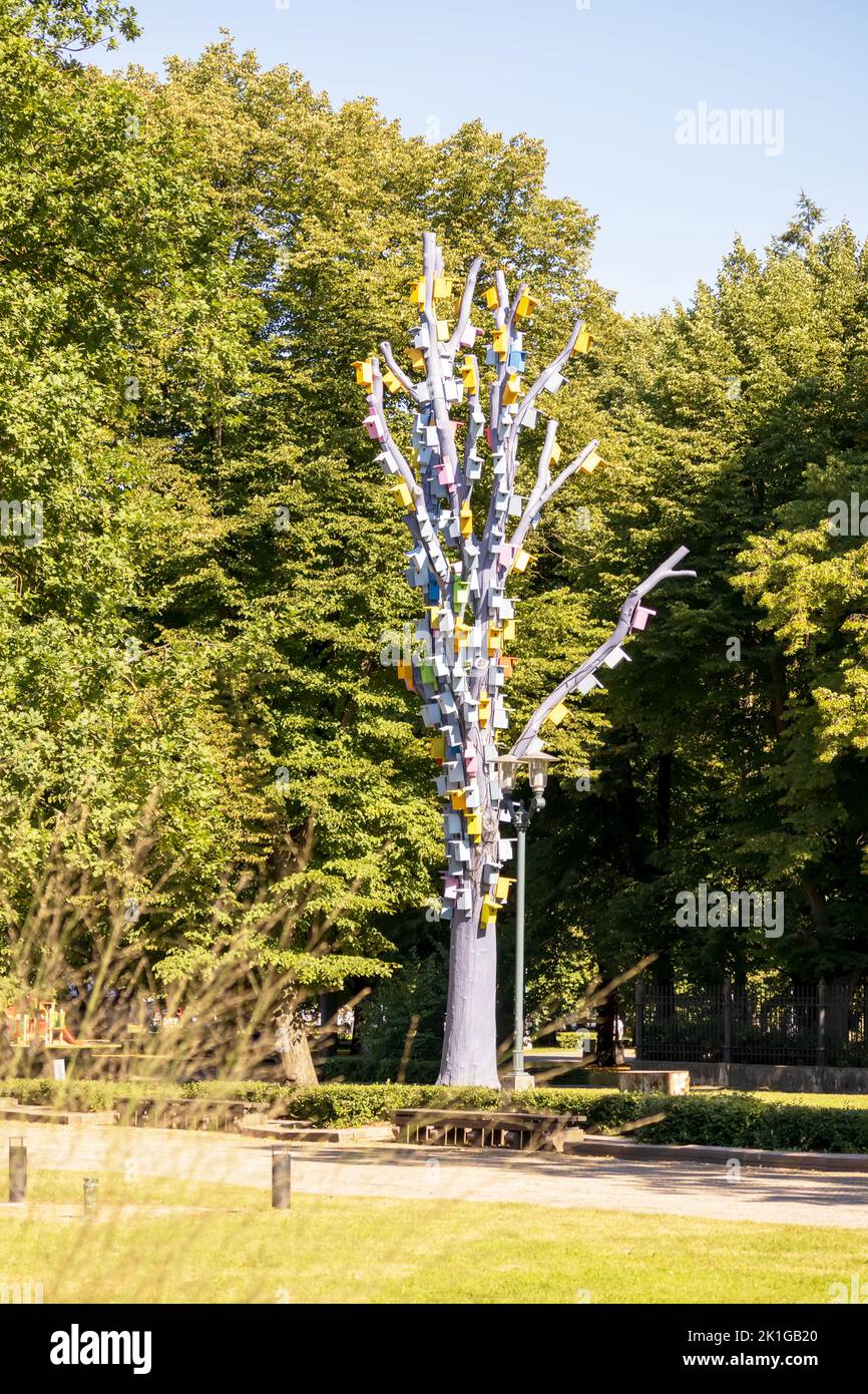 A gray tree full of colored bird cages stacked on top of each other ...