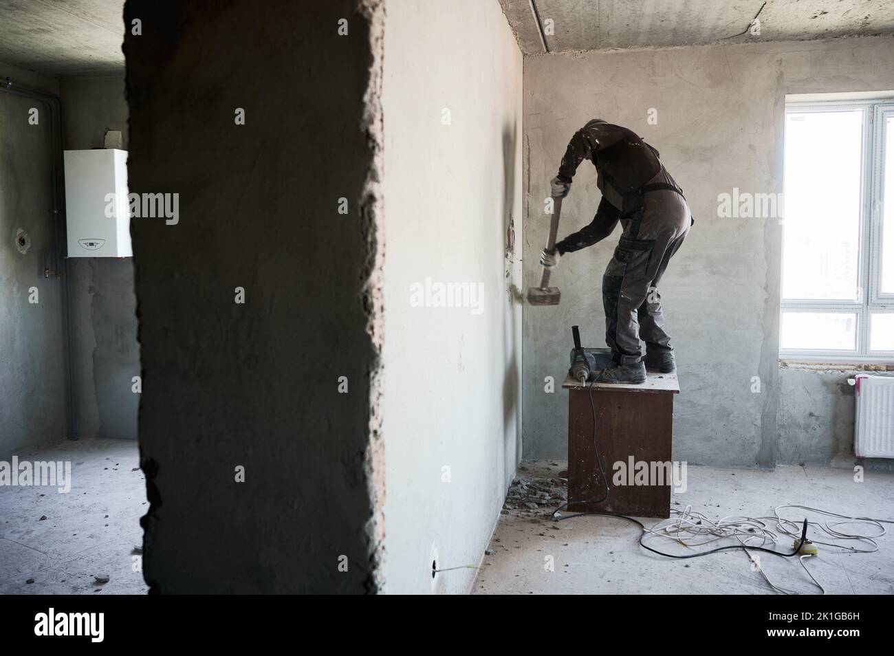 Side view of worker standing on wooden table, holding sledgehammer and ...