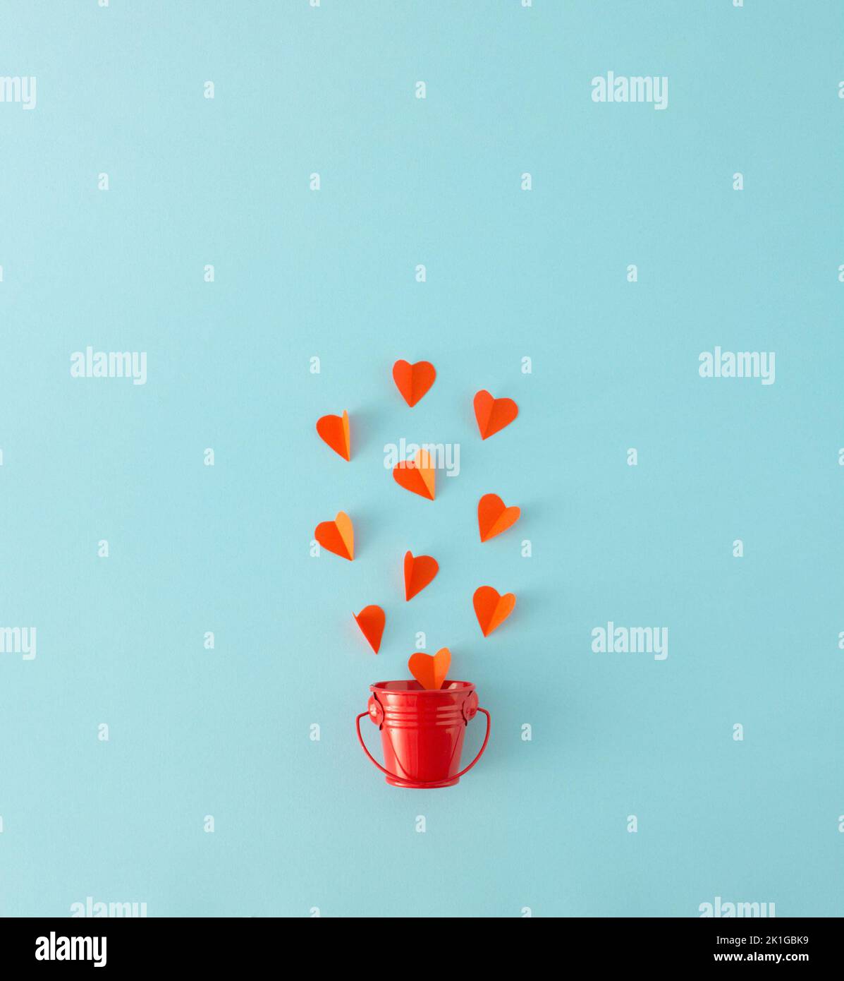 Red paper hearts flying out of the red metal bucket on a blue ...