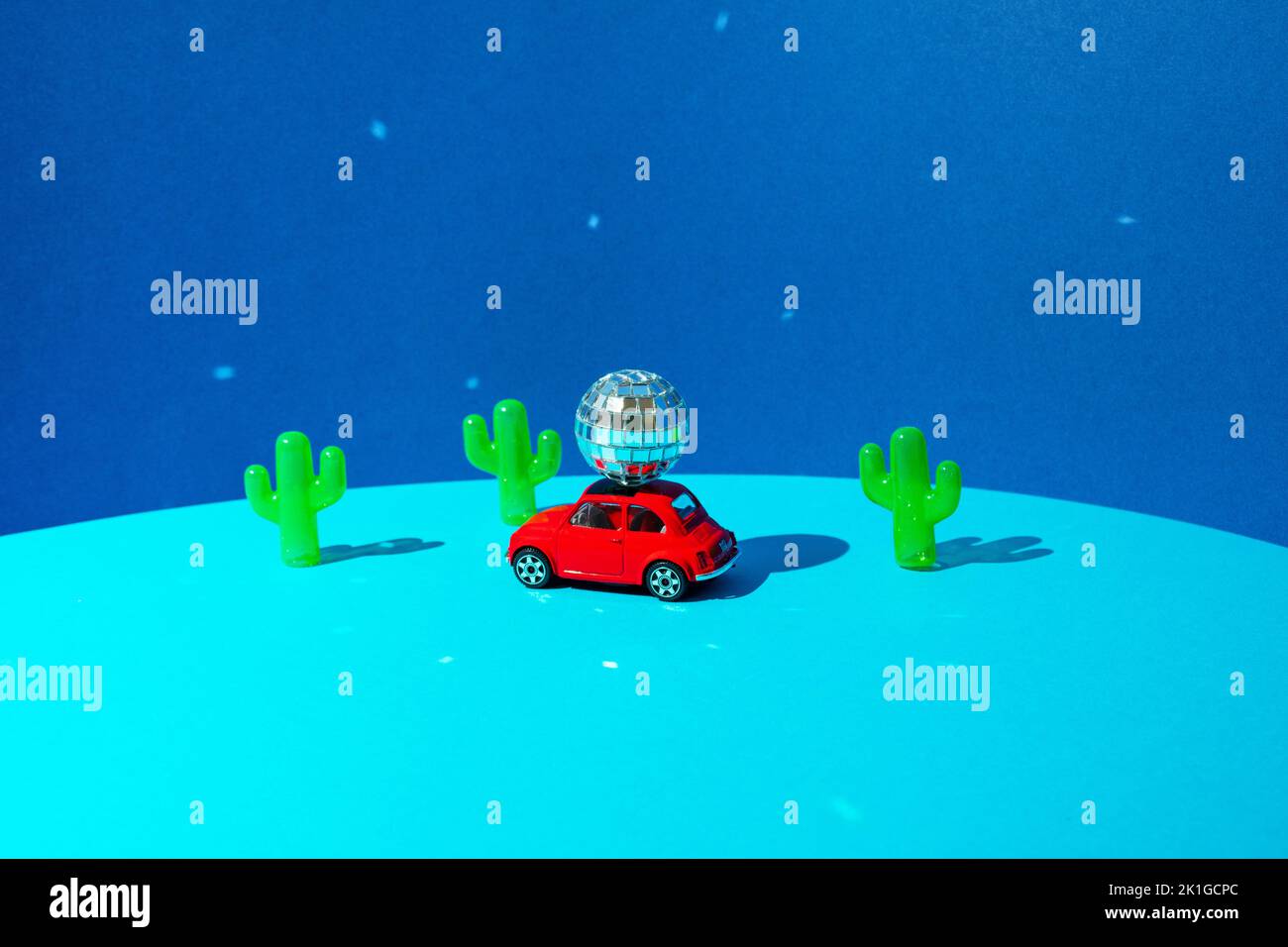 Disco ball on the roof of a moving red car and plastic cacti on the ...