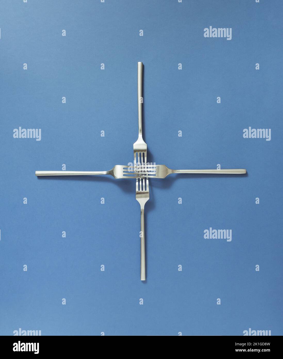 Four silver forks intertwined in the shape of a cross on blue ...