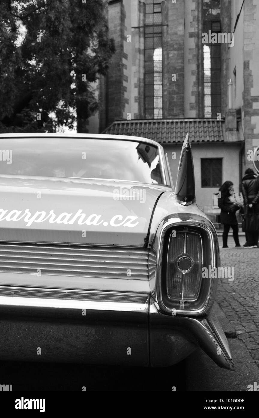 A vertical closeup grayscale back view of an old Cadillac in city ...