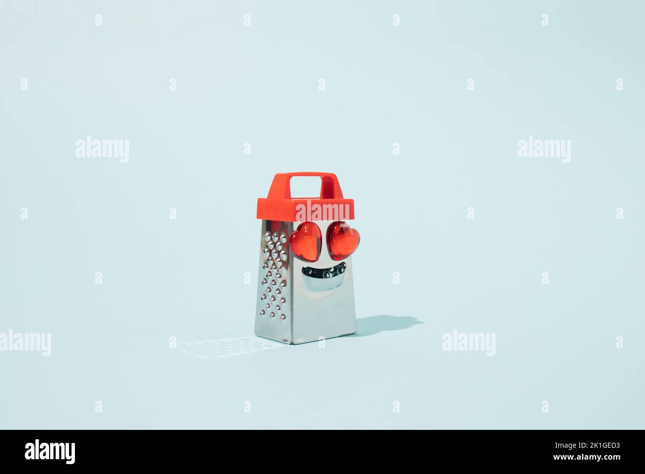 Metal grater with heart-shaped glass eyes on blue background. Minimal ...
