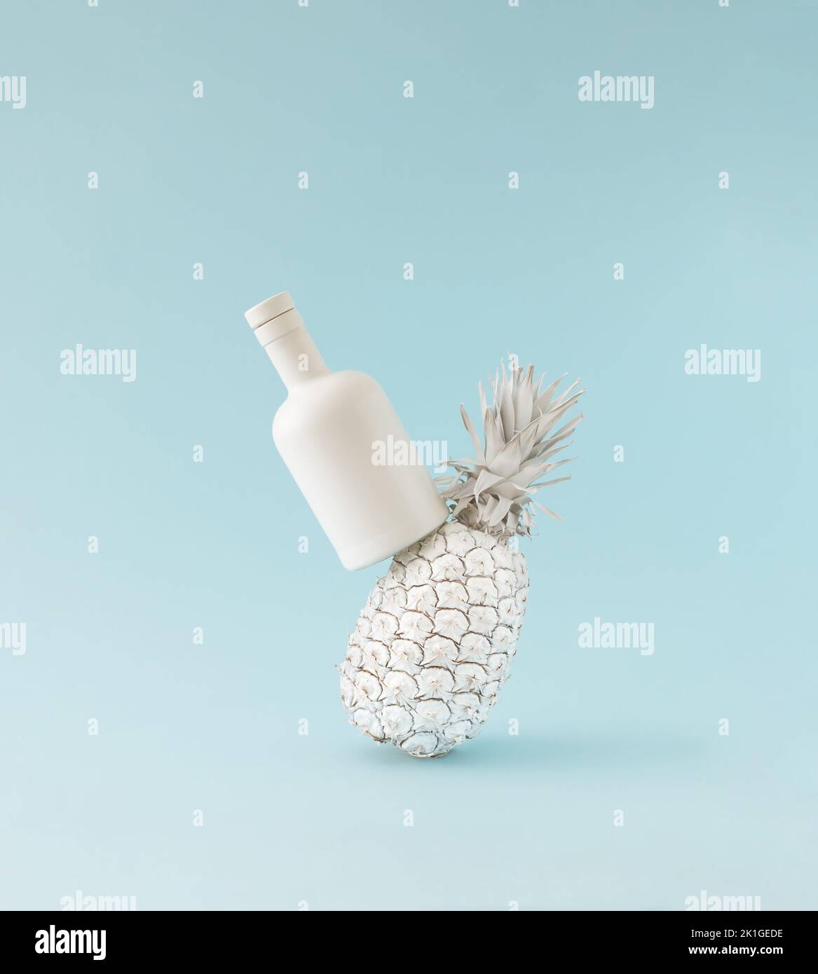 White bottle balancing on white pineapple on blue abckground. Minimal ...