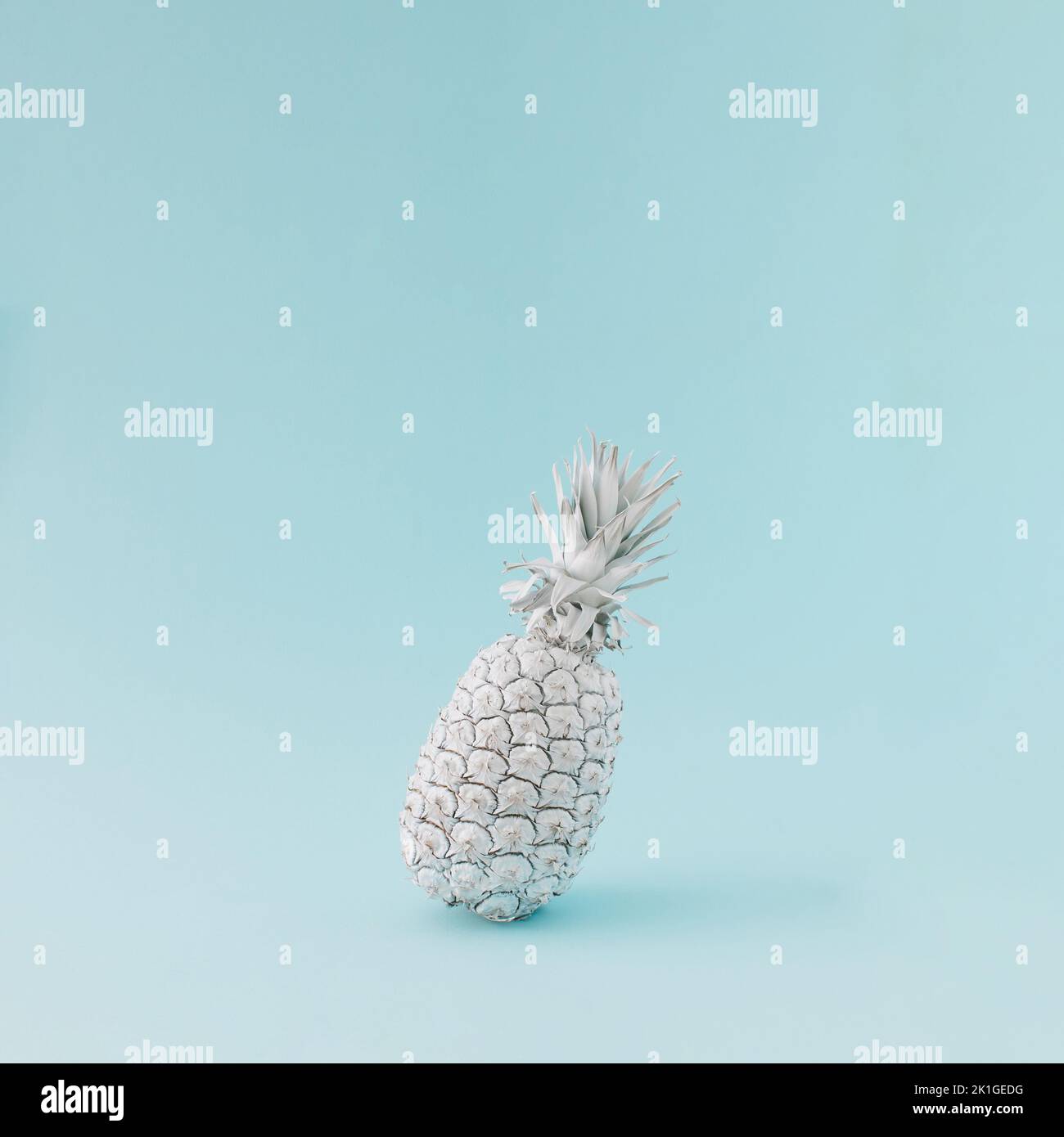 Pineapple colored in white balancing on blue background. Minimal summer ...