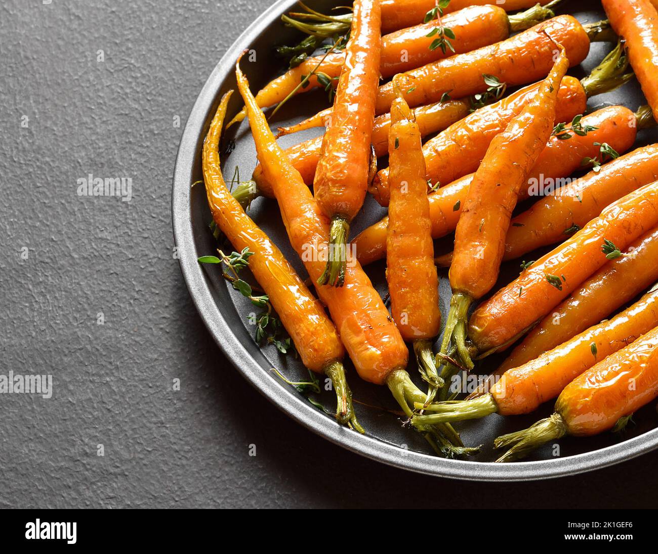 Close up view of roasted honey glazed carrots on plate over dark stone ...
